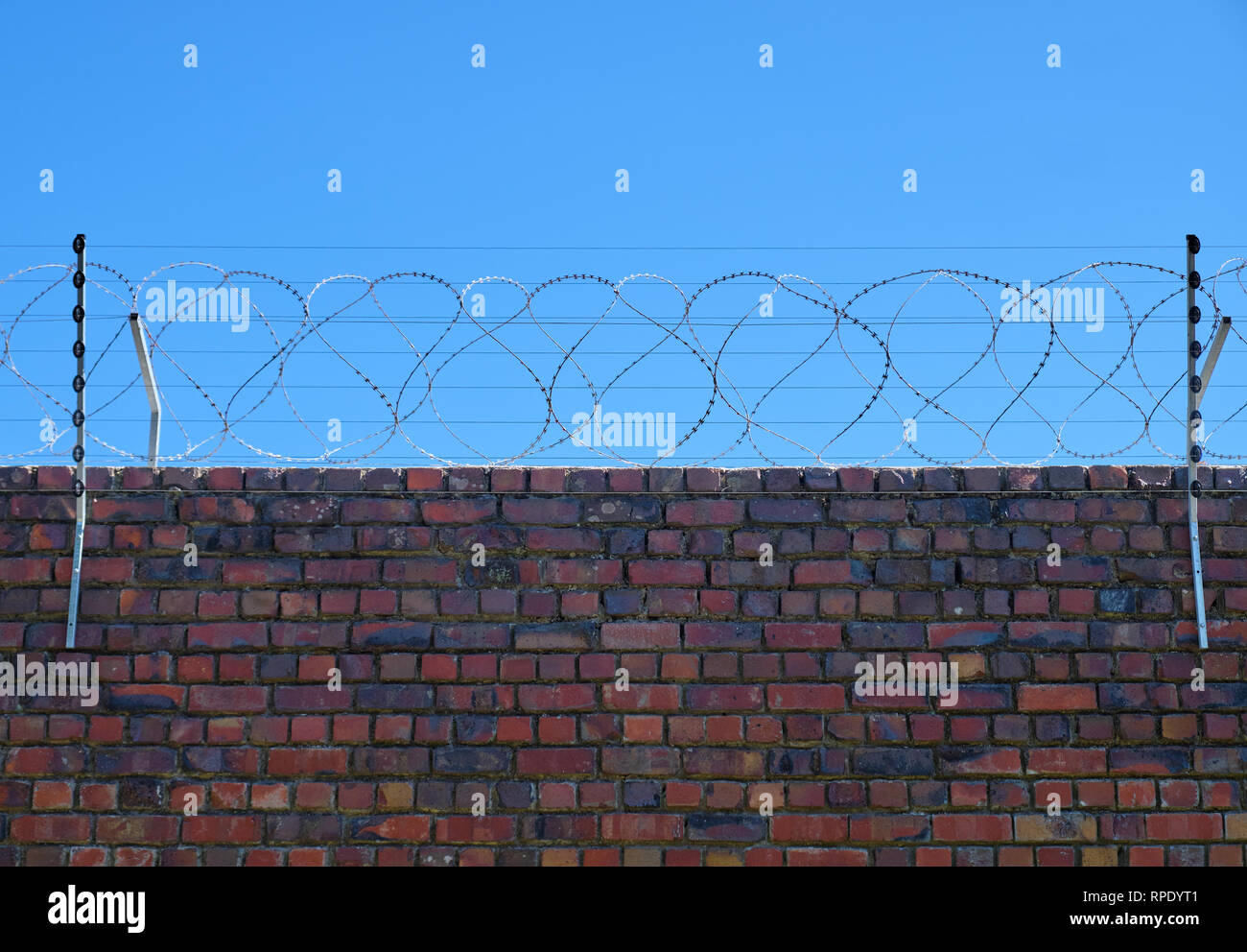 Barb wire and electrical fence at the top of a brick wall against a ...