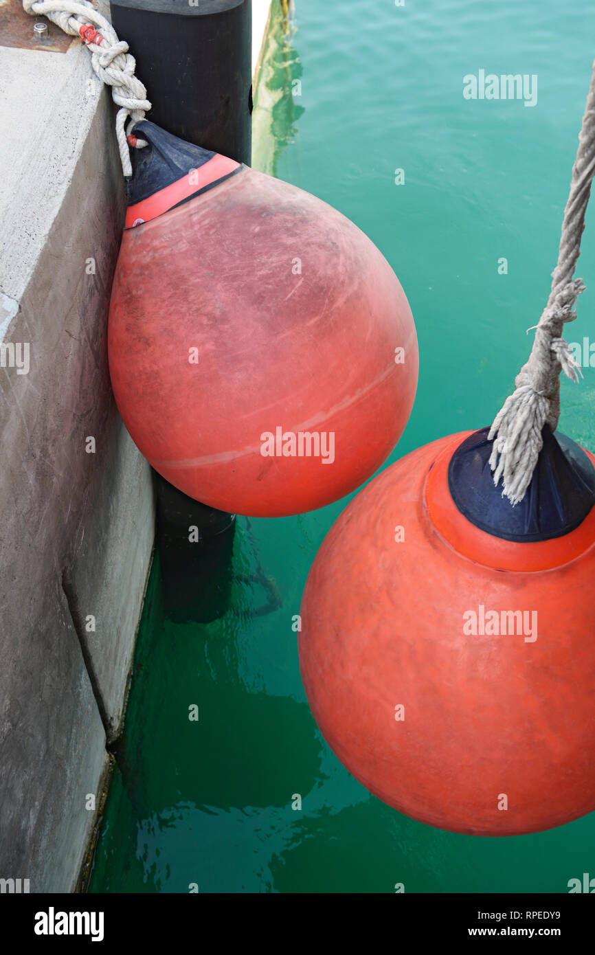 Close-up two red plastic dock mooring fender that are hanging on the ...