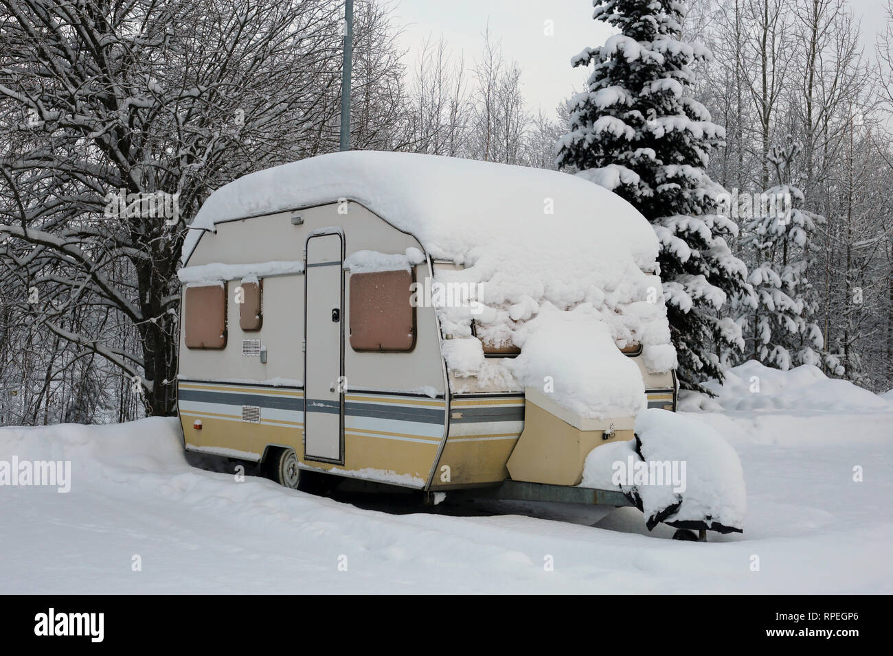 Caravan trailer in a parking lot next to a forest covered with snow ...
