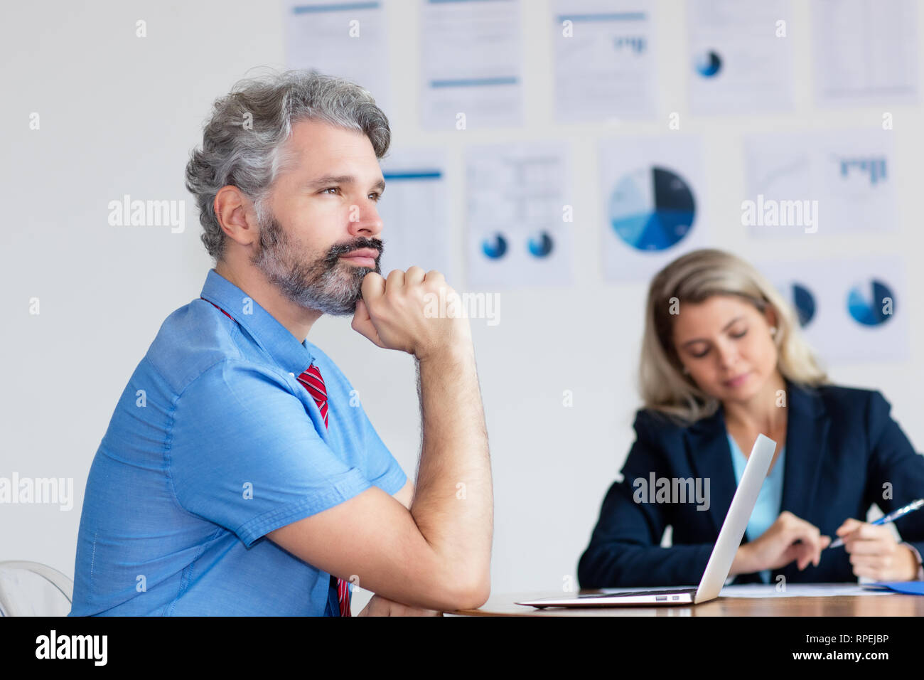 Thinking german businessman with grey hair and computer at desk at ...