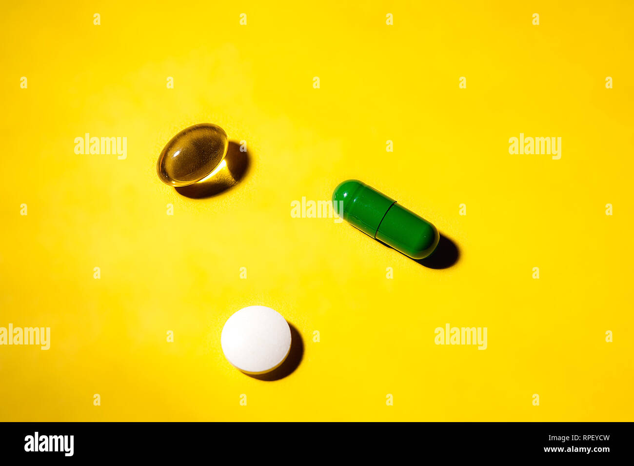 Three colored tablets and capsules on yellow background Stock Photo - Alamy