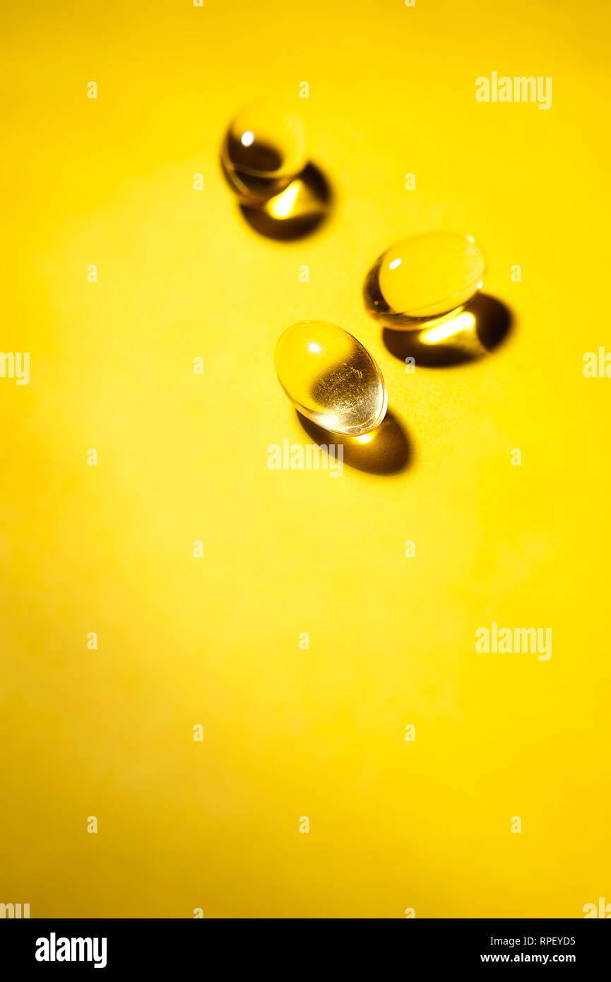 Yellow transparent fish oil pills on yellow background. Vertical image ...