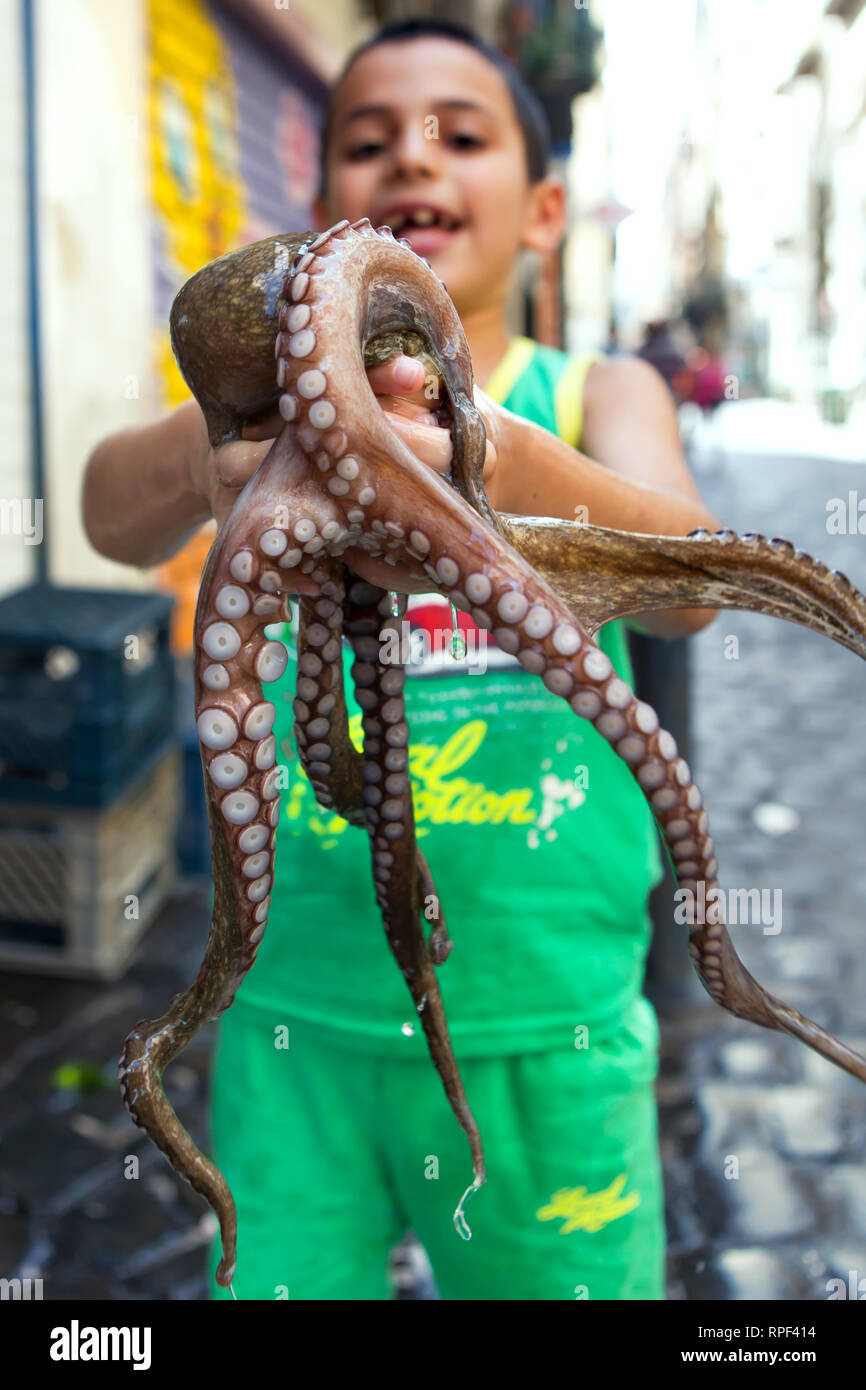 NAPLES - A boy shows off an octopus in front of a fish shop in the ...