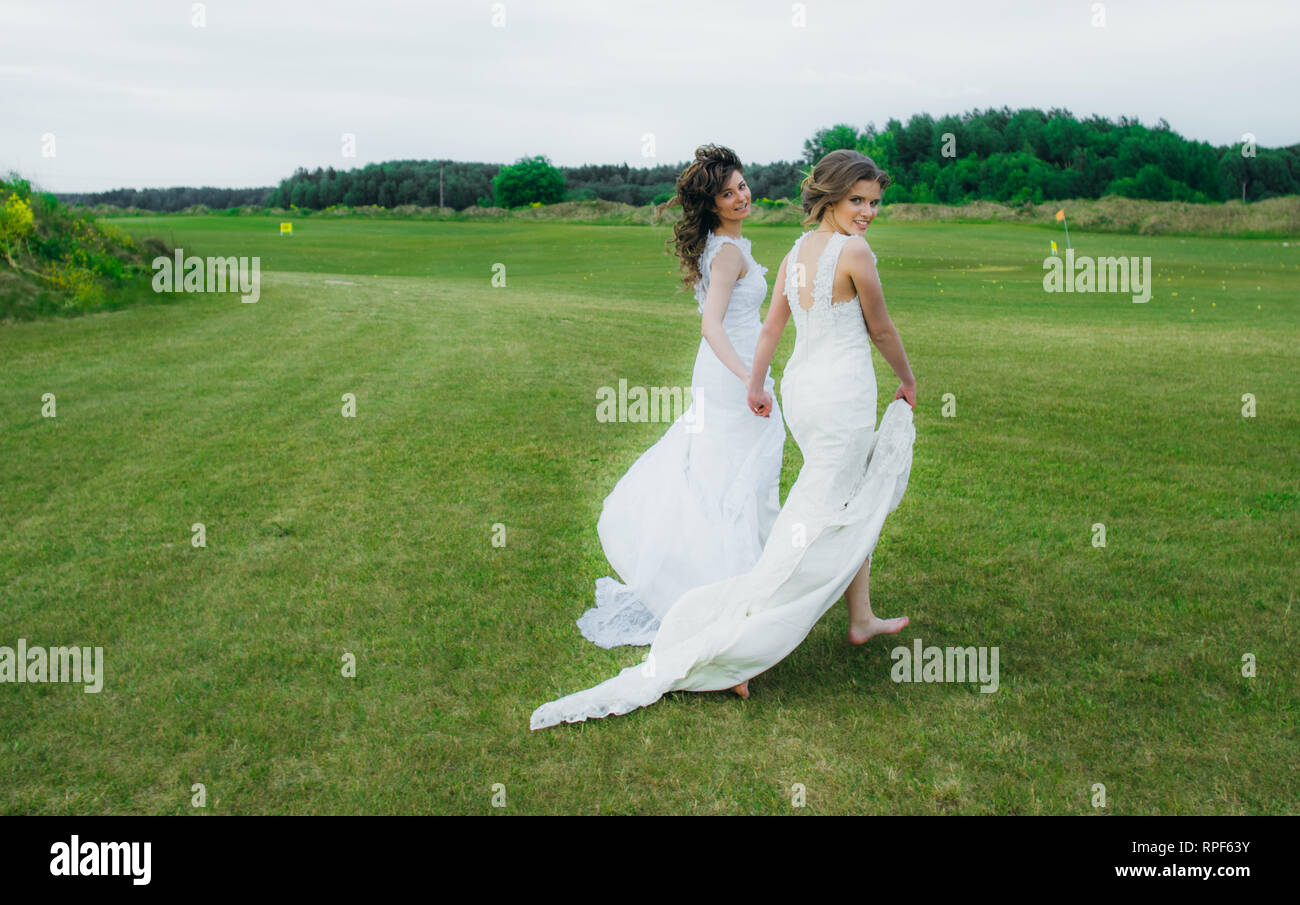 Two beautiful brides walking on the green field of the golf club Stock ...