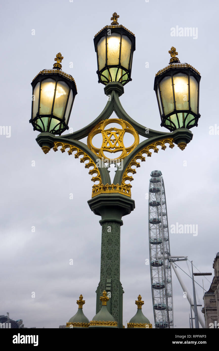 Ornate triple headed cast iron lamp post with gas lights lit on ...