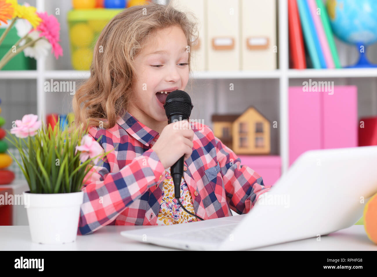 Little girl in checkered shirt singing karaoke with laptop at her room ...