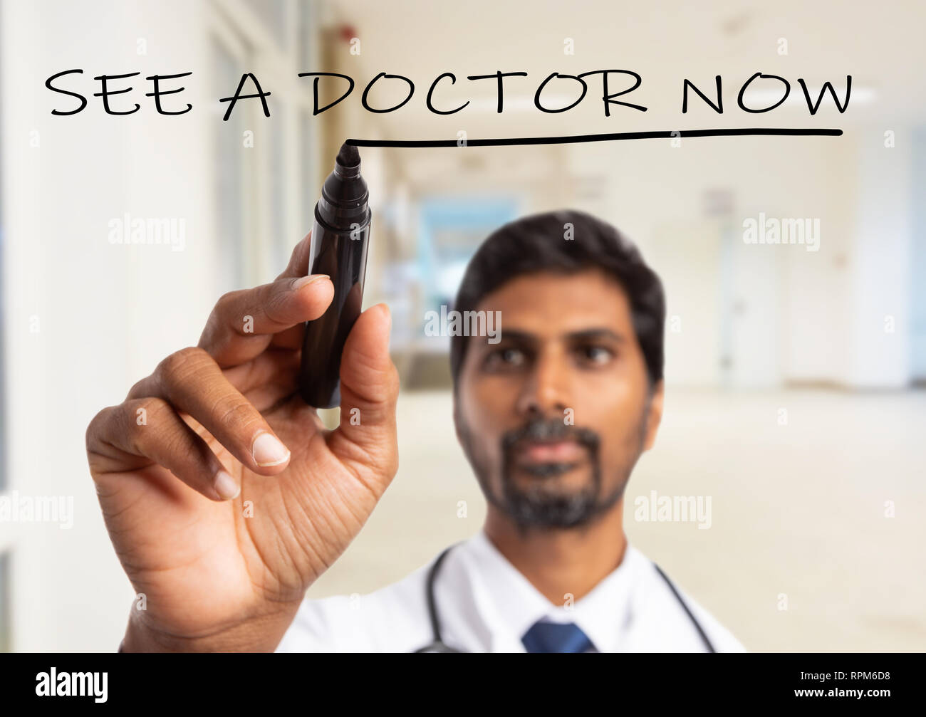 Close-up of male indian doctor underlining see a doctor now text on ...