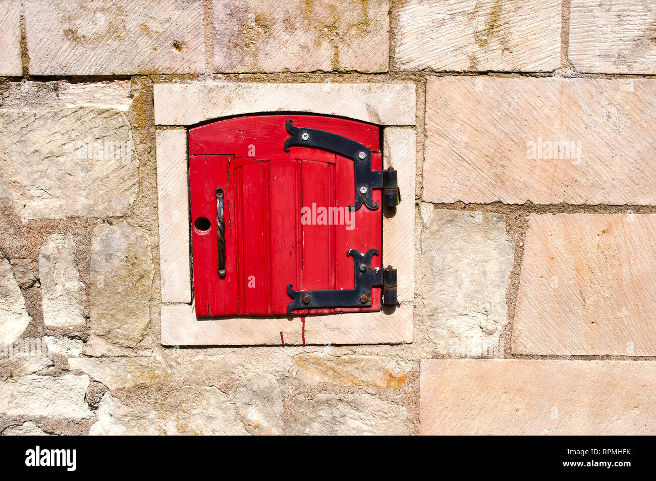 One small arched red door with metal higes on a stone wall Stock Photo ...