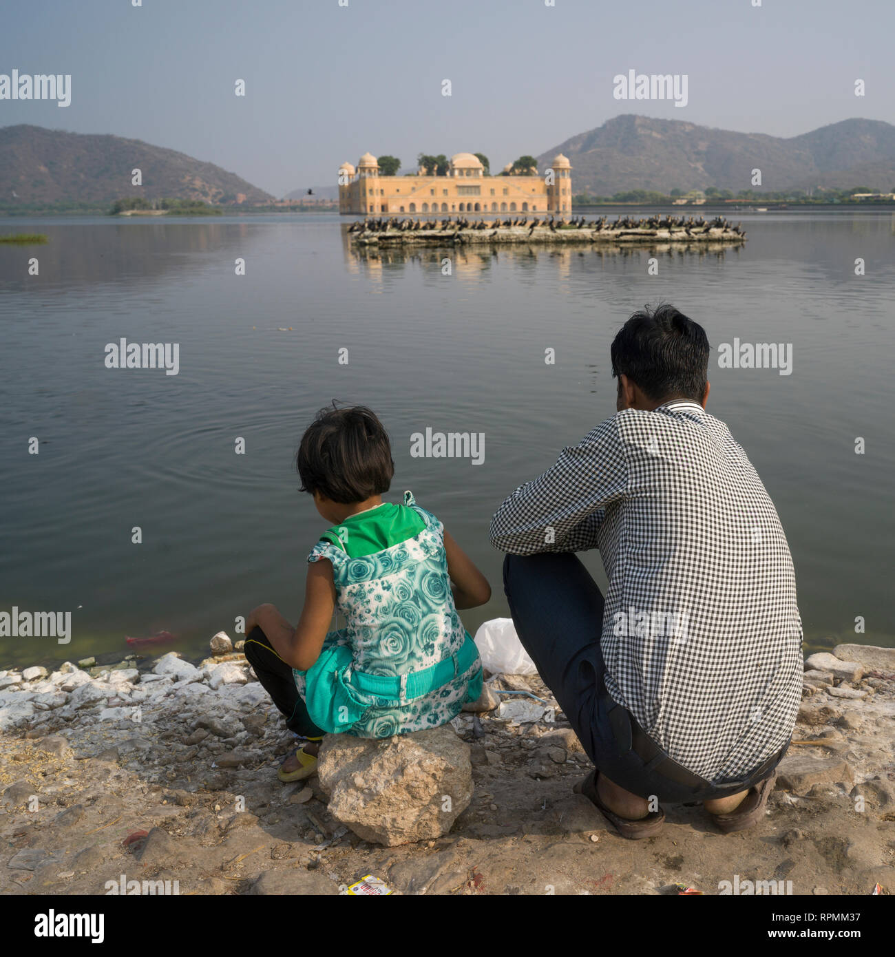 Man sitting at the lakeside with his daughter with Jal Mahal Grand ...