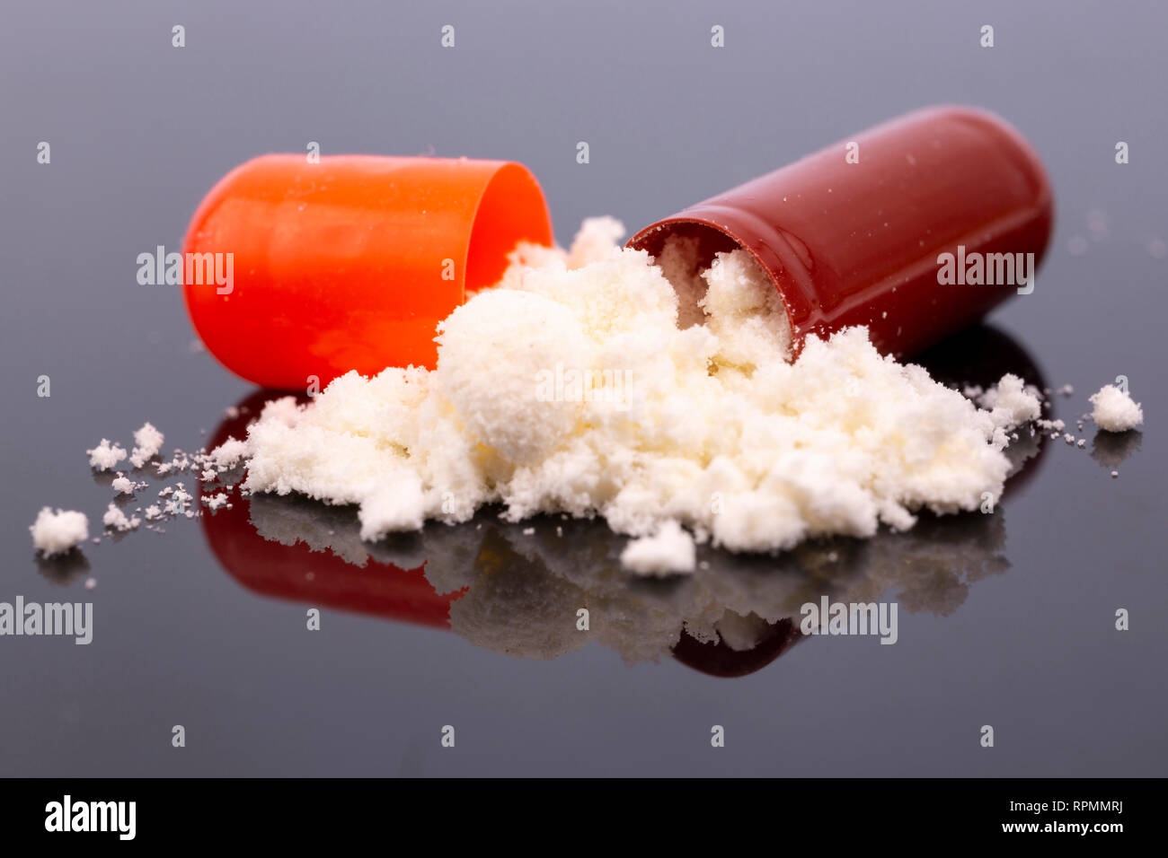 Single red capsule and white powder isolated on black reflective ...