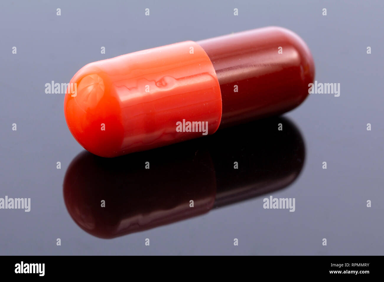 Single red capsule isolated on black reflective surface. Global ...