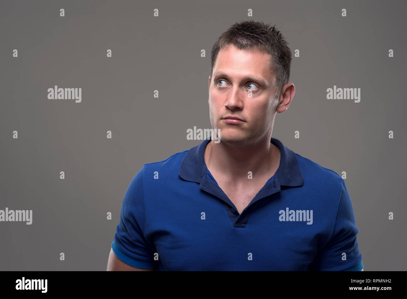 Portrait of confused young adult man looking up at copy space over gray ...