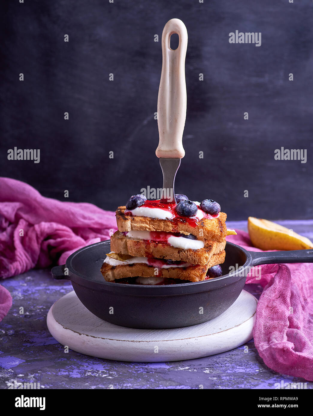 French toast with berries, syrup and sour cream in a black cast-iron ...