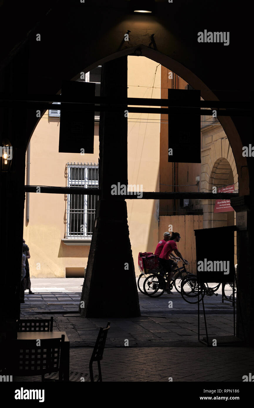 People on a bicycle framed by the arch of a portico in downtown Bologna ...
