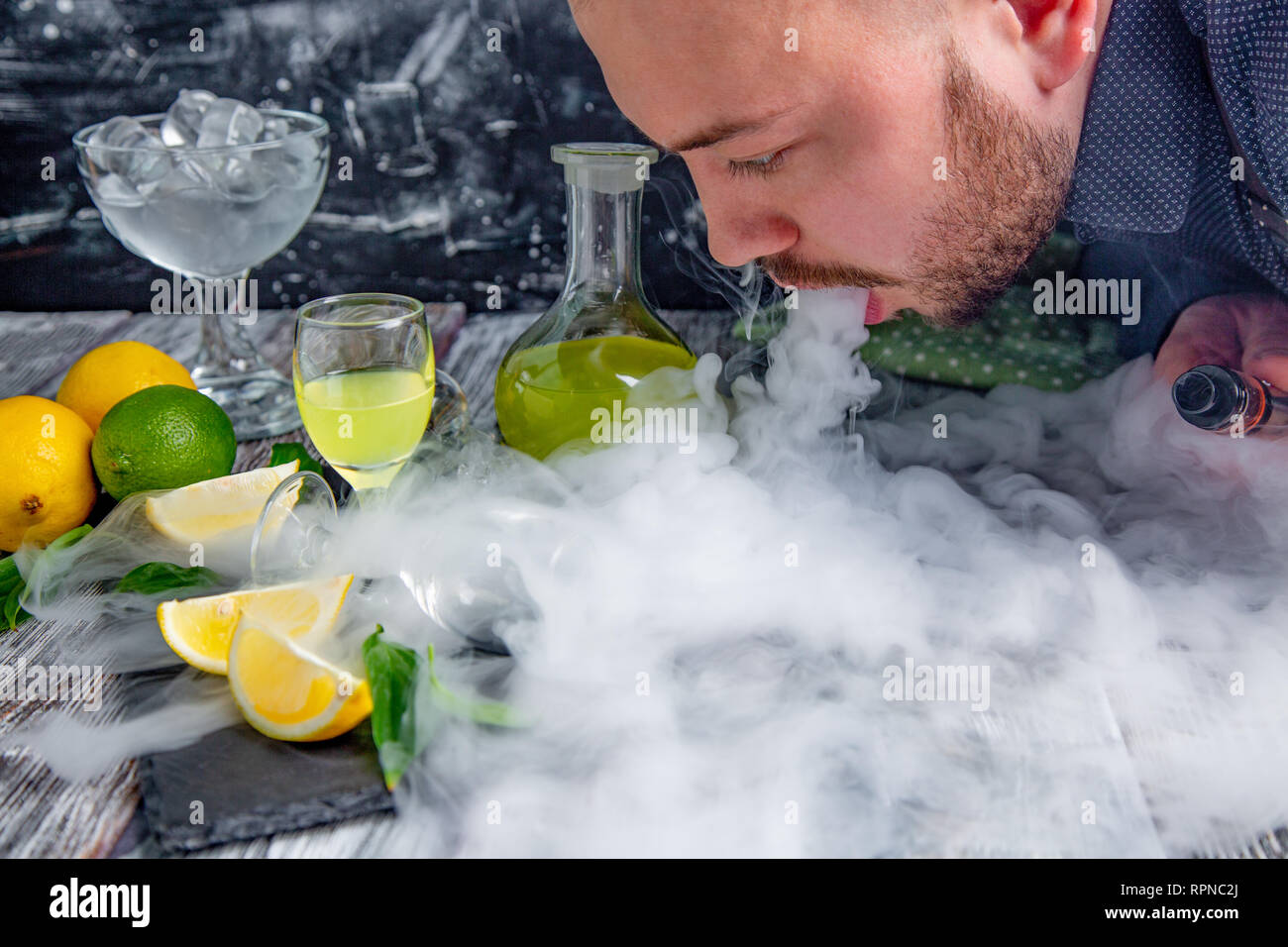 man lets out steam from a mouth on a table served with limoncello Stock ...