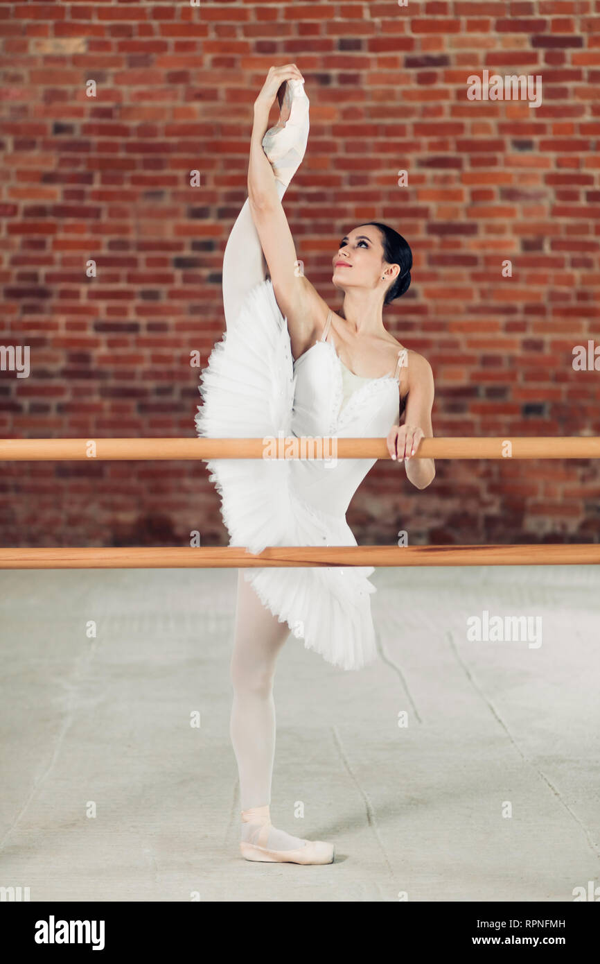 elegant young smiling woman in tutu stretching legs in dance class ...
