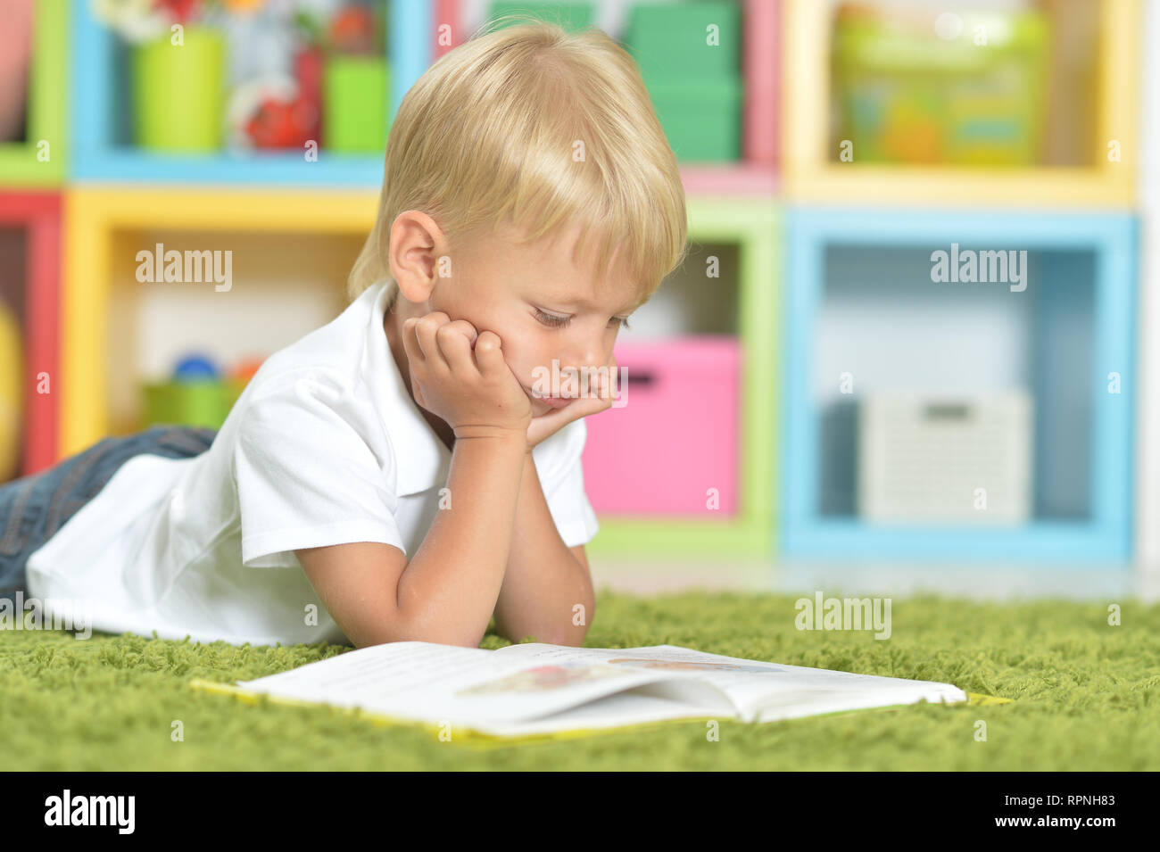 Cute little boy reading a book while lying on floor Stock Photo - Alamy