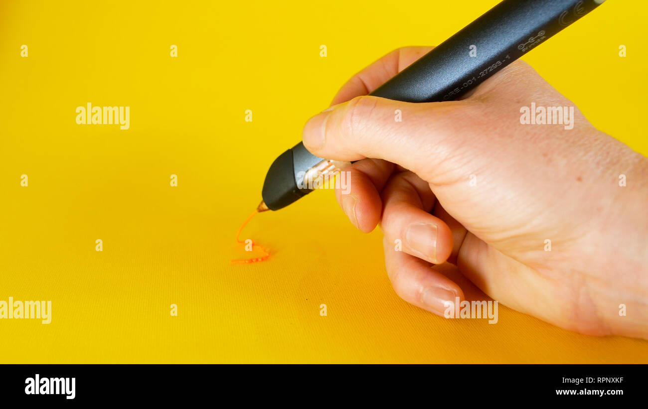 a man's hand draws with a 3d printer pen on a yellow background ...