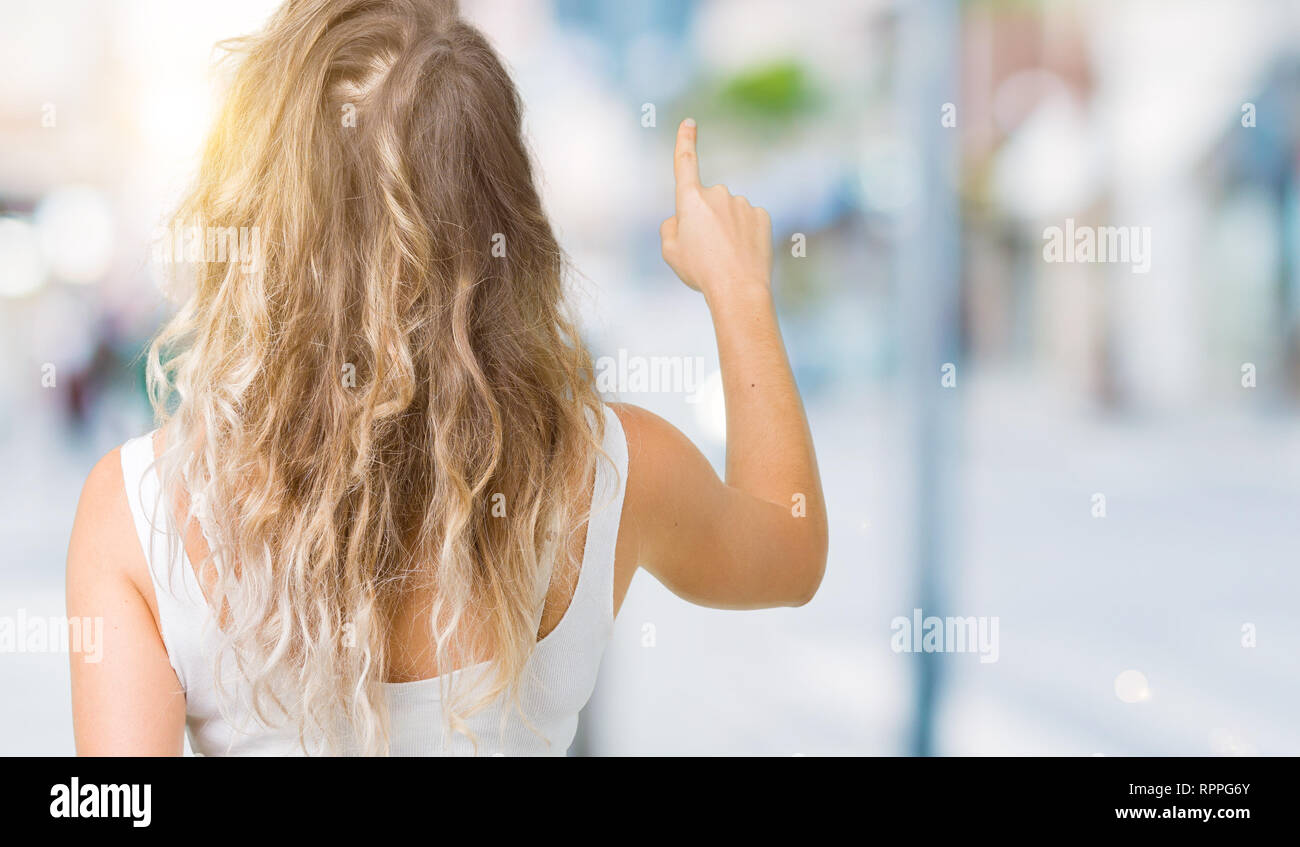 Beautiful young blonde woman over isolated background Posing backwards ...