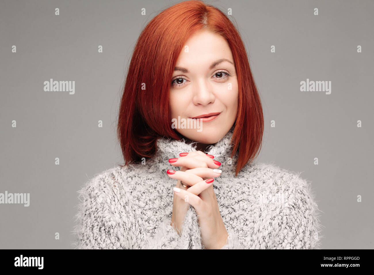 Charming woman with ginger hair smiling and putting hands together ...