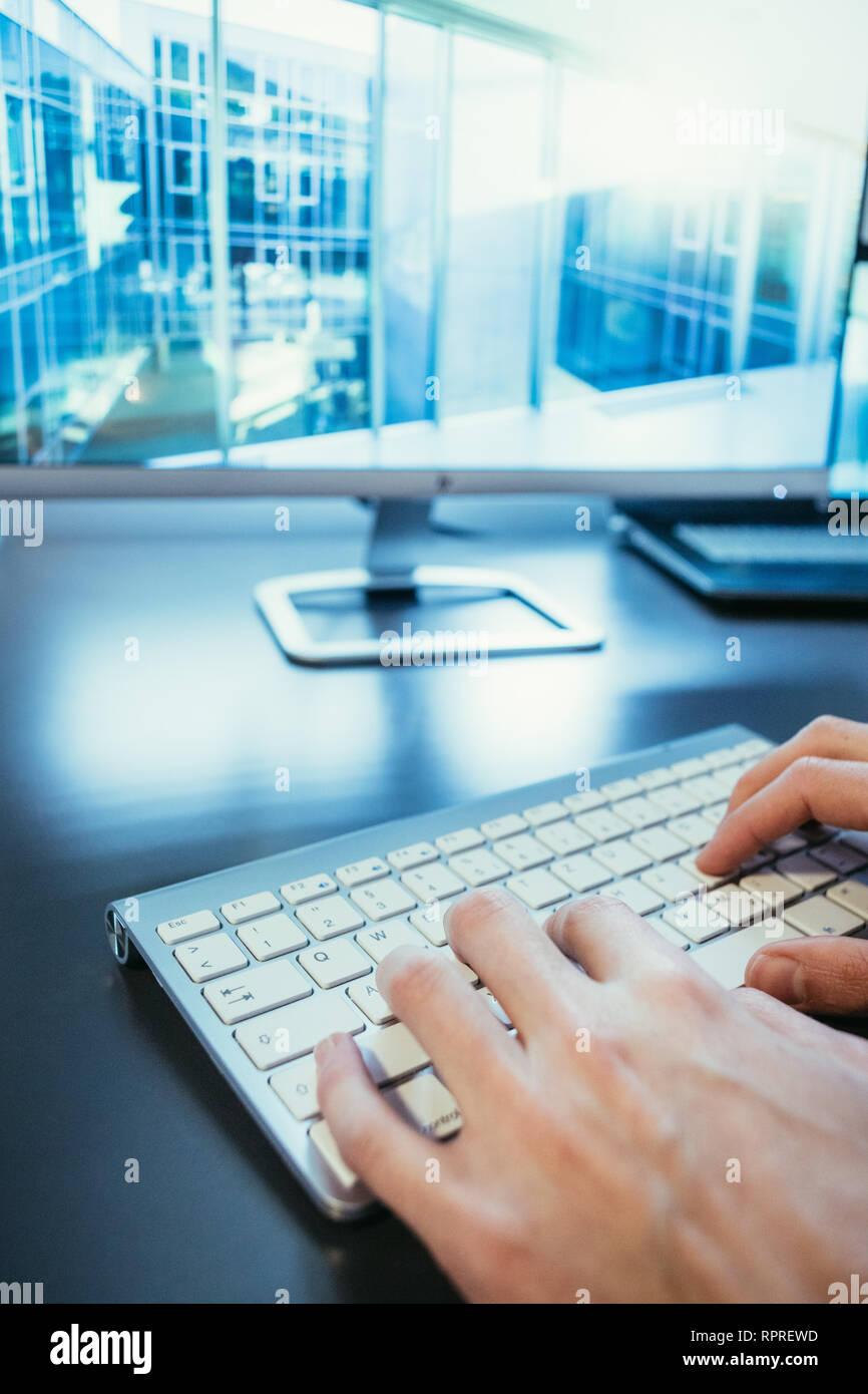 Hands are typing on a white keyboard, screen in the blurry background ...