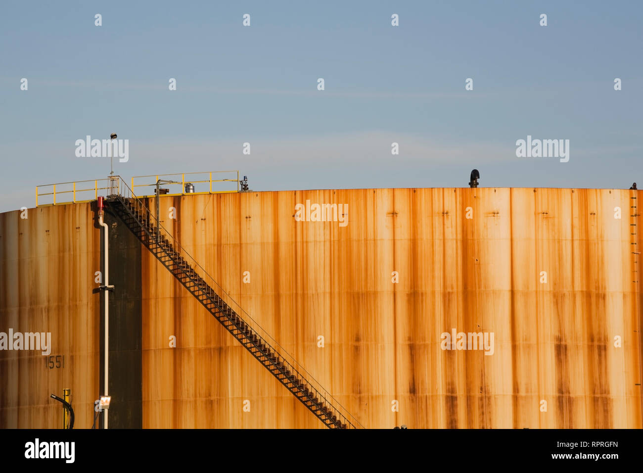 Rusted oil storage tank with black metal staircase at an oil and gas ...