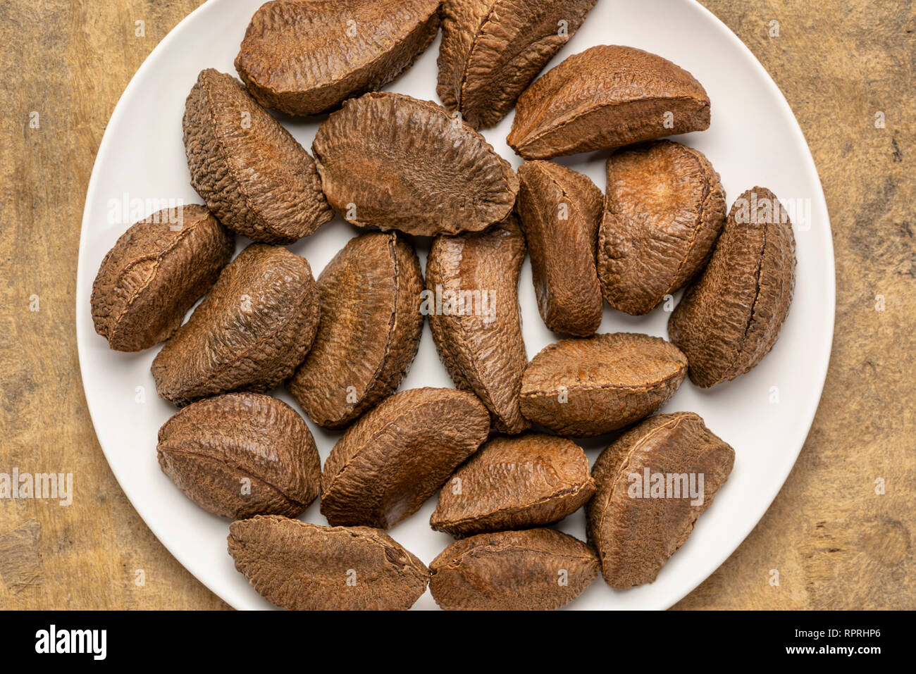 Brazilian nuts in shells on a white plate against textured bark paper ...