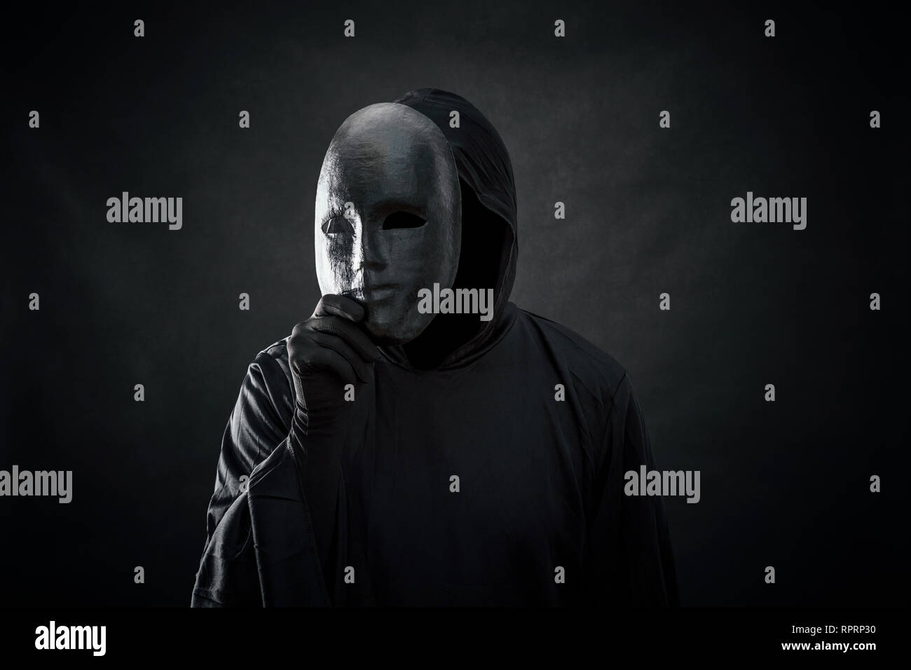 Scary figure in hooded cloak with mask in hand Stock Photo - Alamy