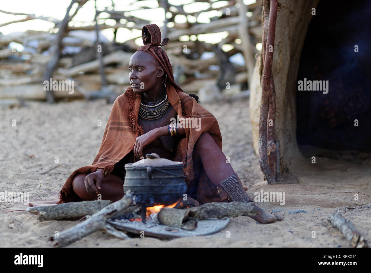 Himba woman sitting in front of the hut making dinner on fire in a ...