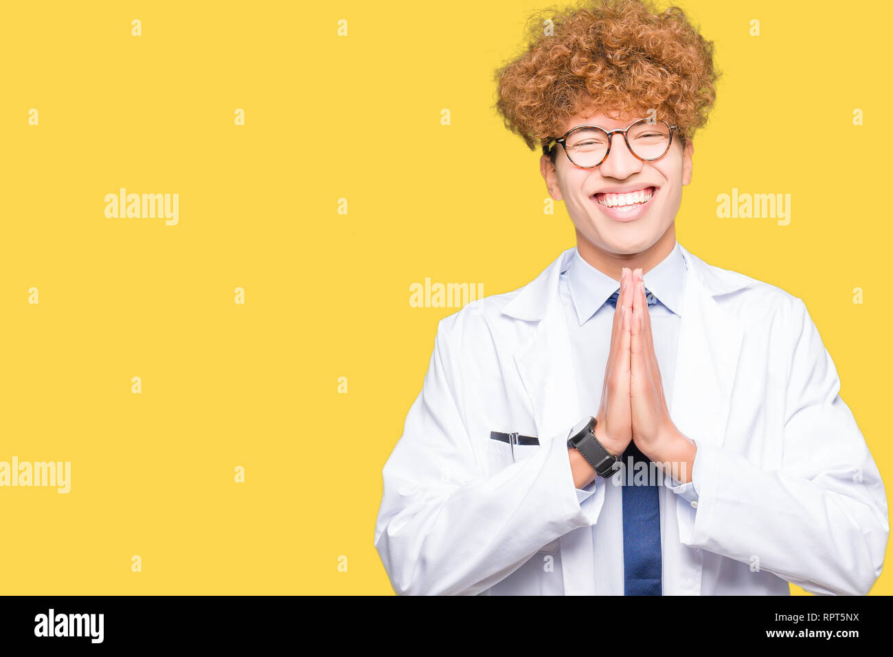 Young handsome scientist man wearing glasses praying with hands ...