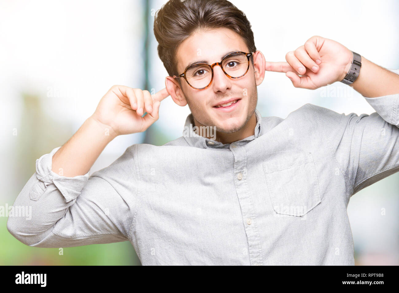 Young handsome man wearing glasses over isolated background Smiling pulling ears with fingers ...