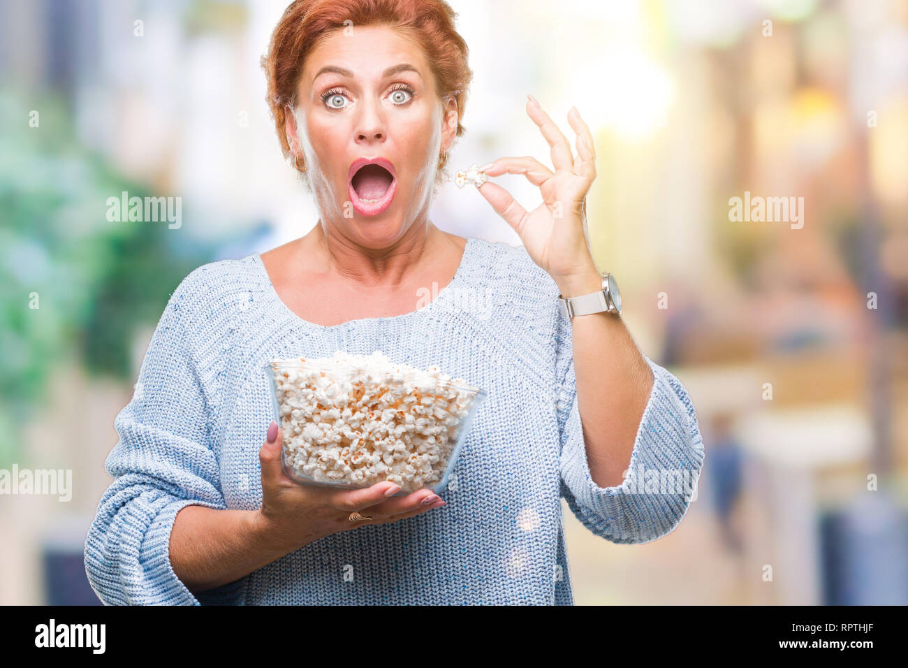 Atrractive senior caucasian redhead woman eating popcorn over isolated ...