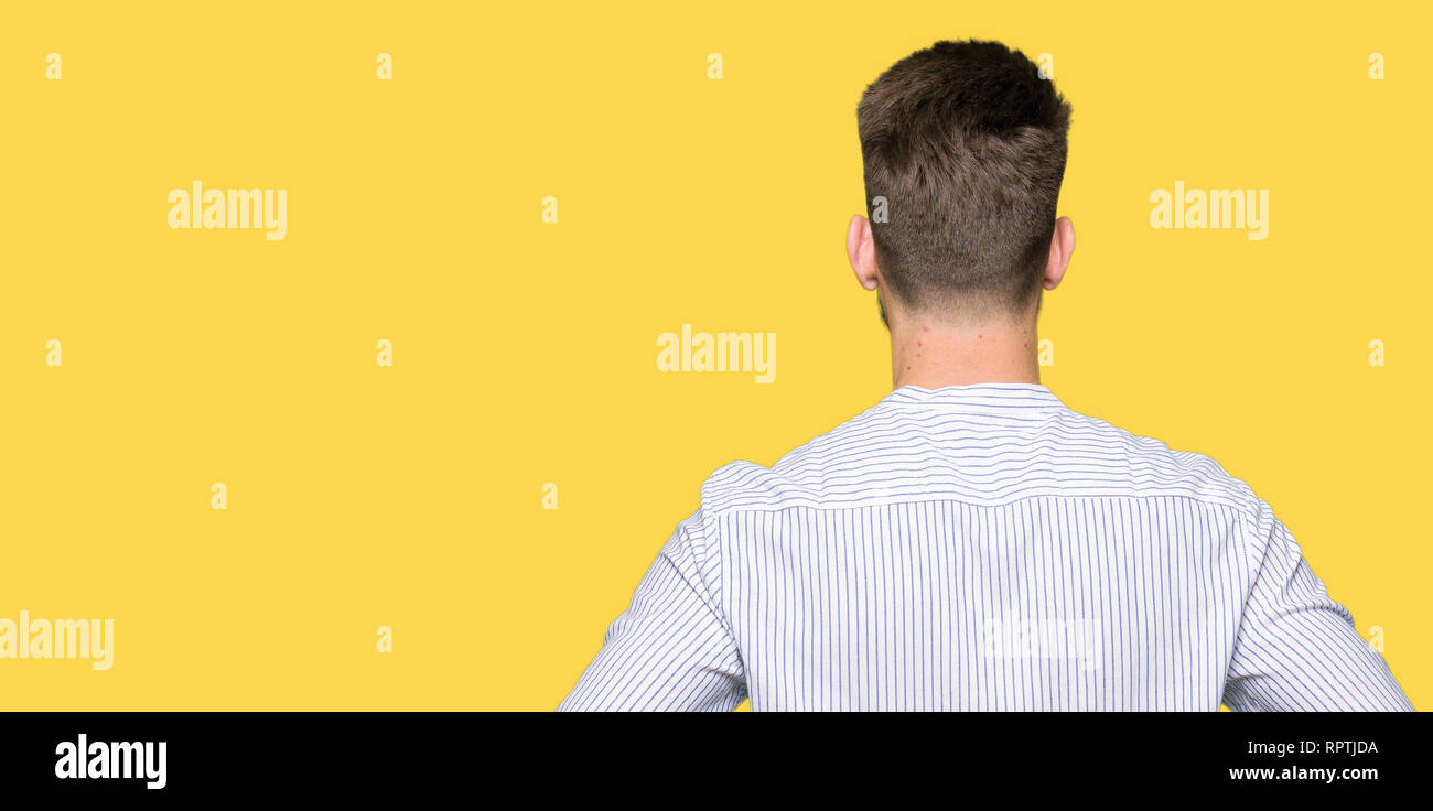 Young handsome man standing backwards looking away with arms on body ...