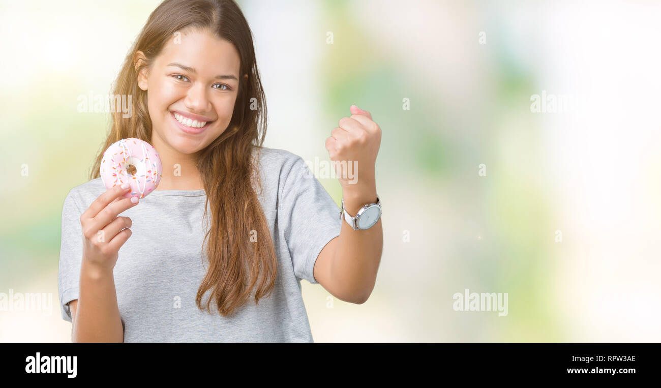 Young beautiful woman eating pink donut over isolated background ...