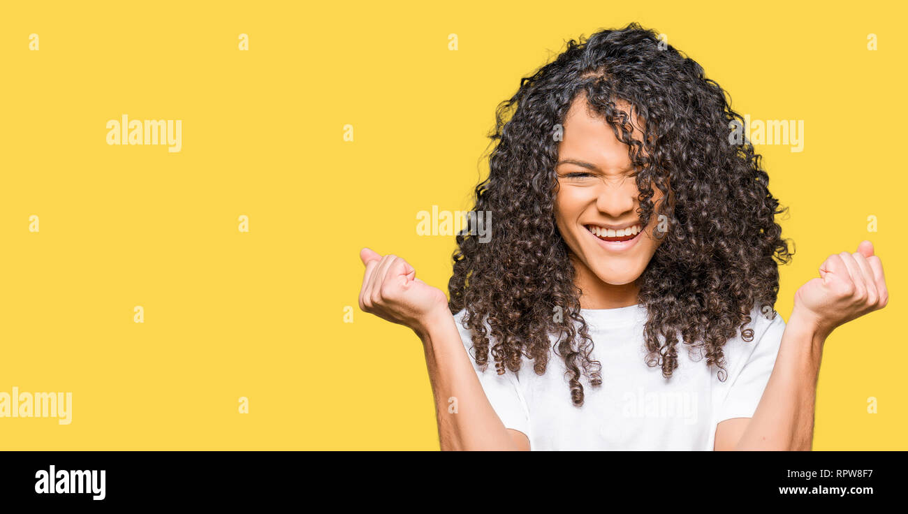 Young beautiful woman with curly hair wearing white t-shirt celebrating ...