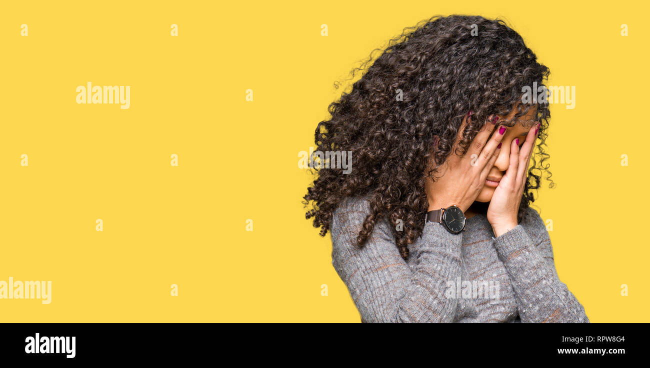 Young beautiful woman with curly hair wearing grey sweater with sad ...