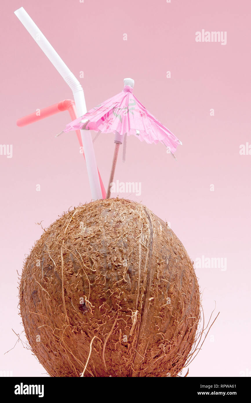 Coconut with drinking straw and umbrella on pink background with copy ...
