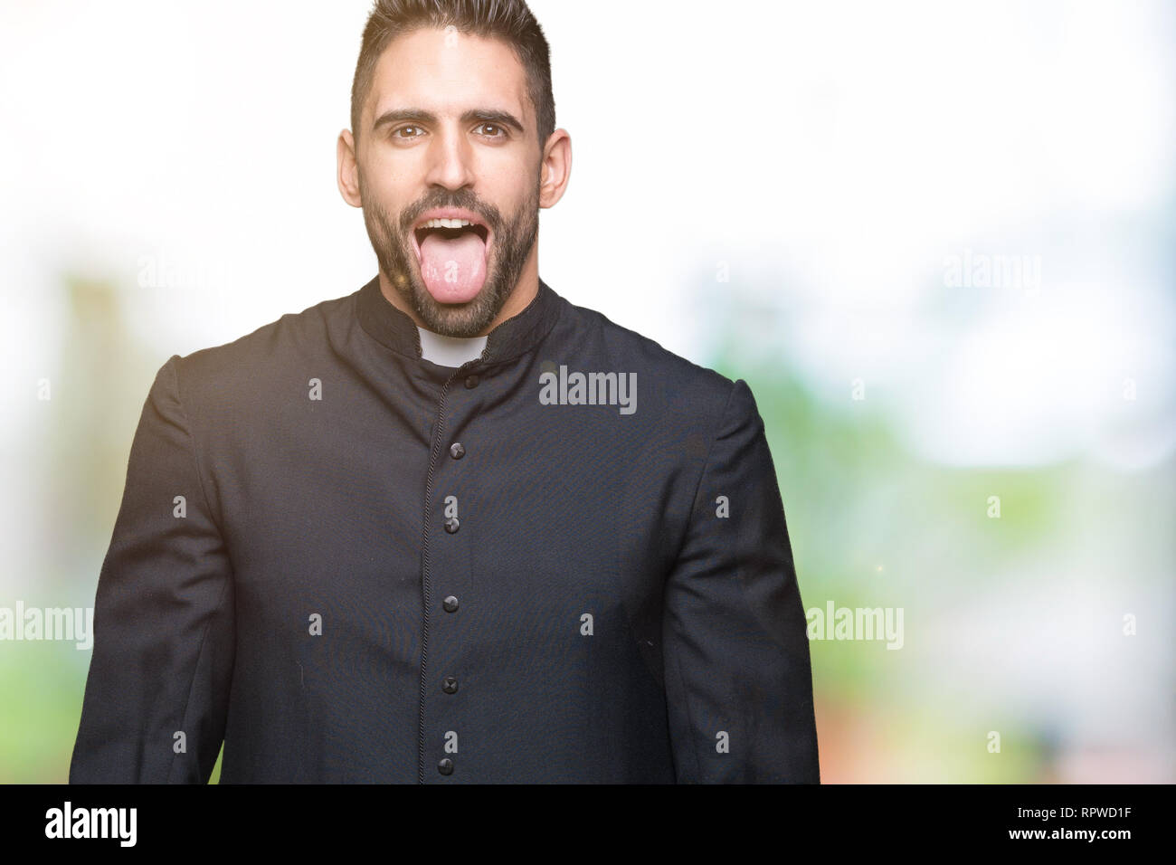 Young Christian priest over isolated background sticking tongue out ...