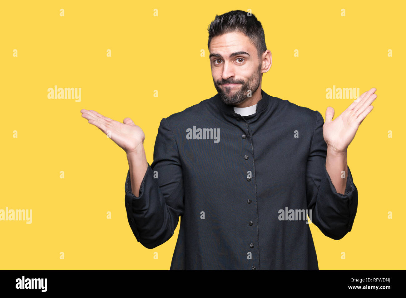 Young Christian priest over isolated background clueless and confused ...