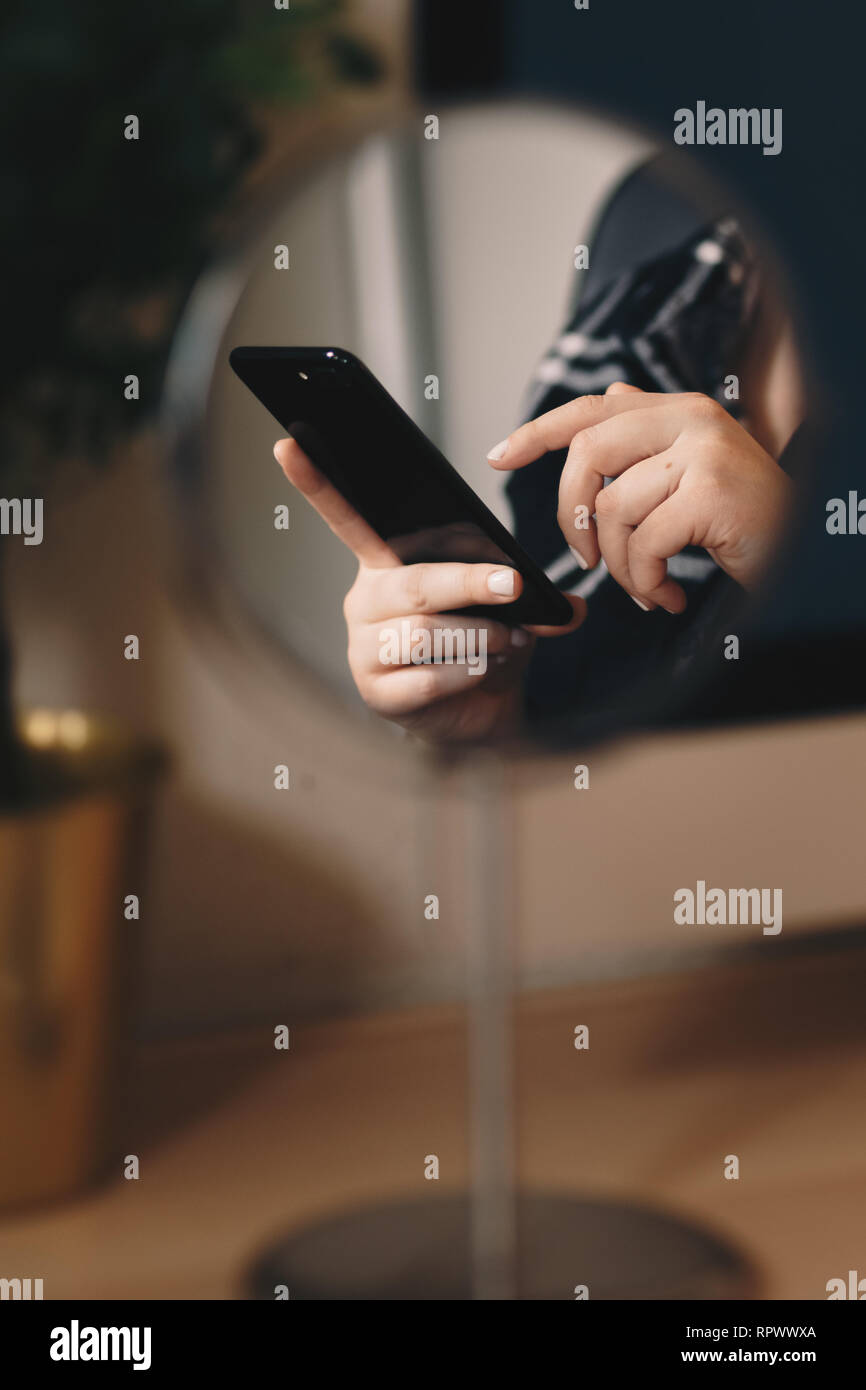 reflection of a woman's hands in a cosmetic mirror. typing on a smart ...