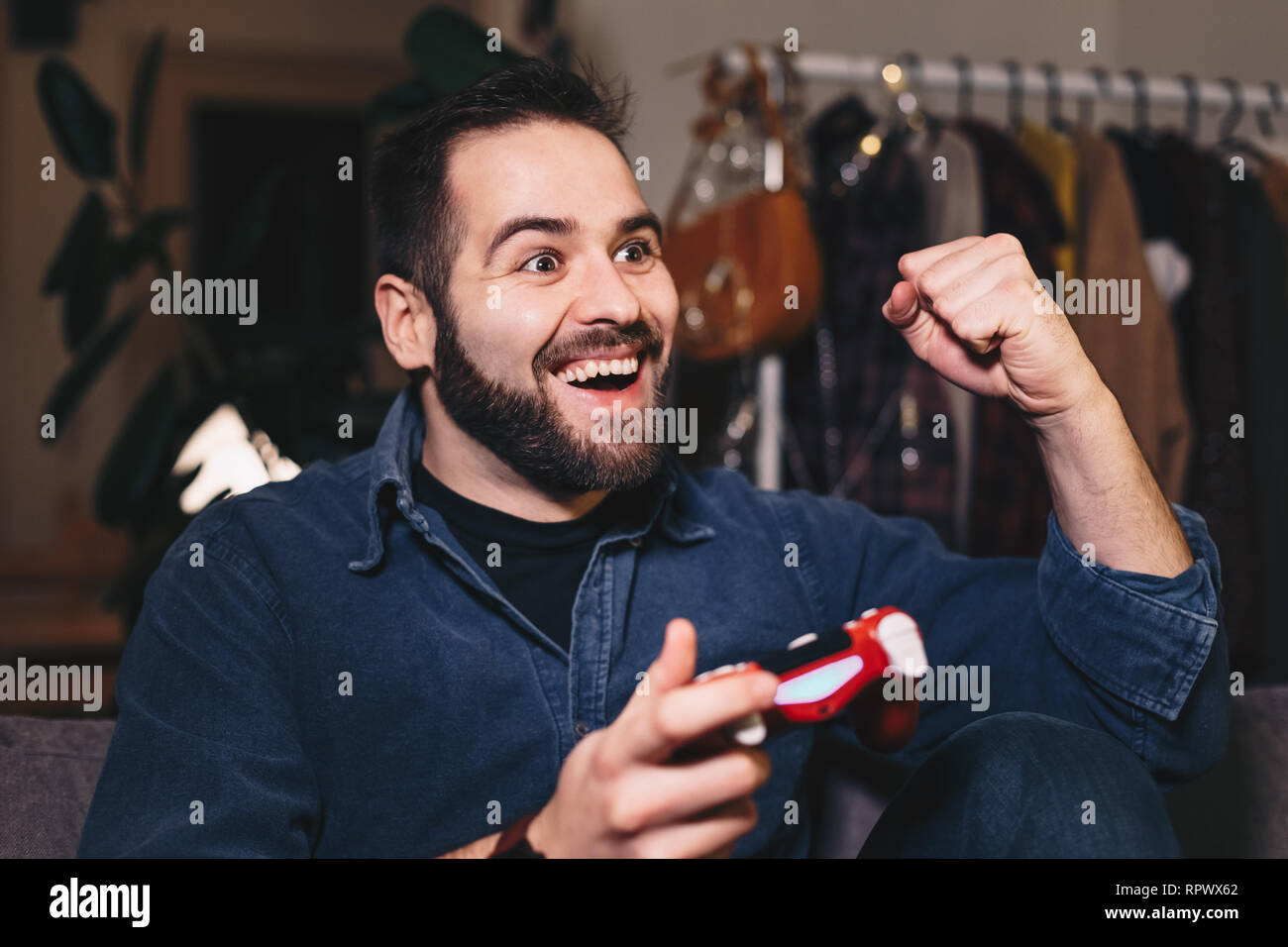Portrait of a young man playing a video game in his living room, happy ...