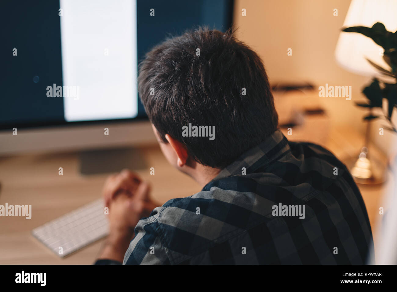 Back view of a young man working from home office, looking at the ...