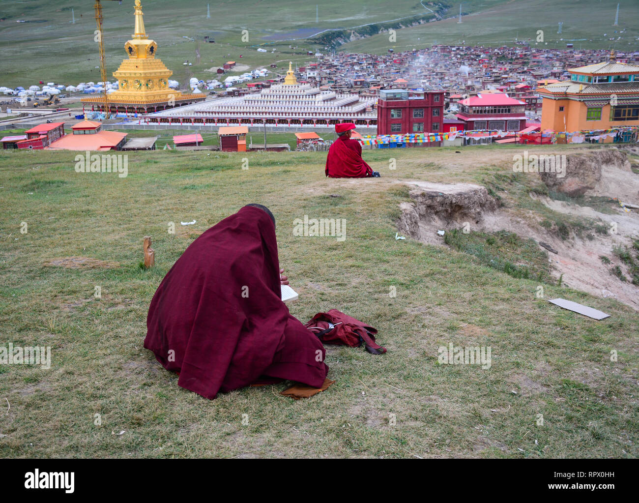 Tibetan monks sitting on the hill and looking at Yarchen Gar in Sichuan ...