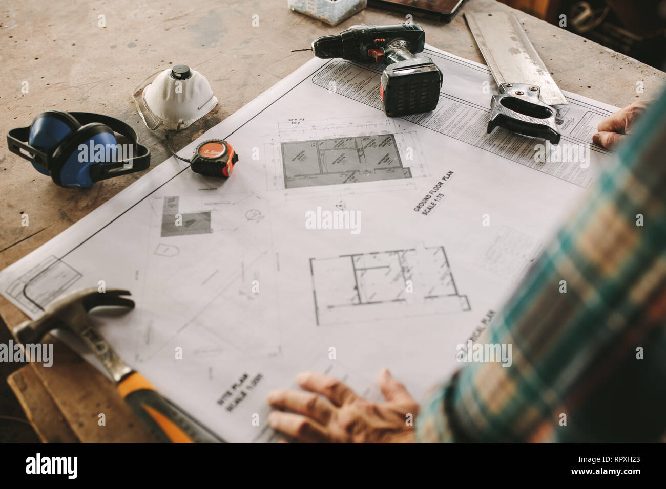 Carpenter reading a floor plan with his tools lying by. Building plan ...