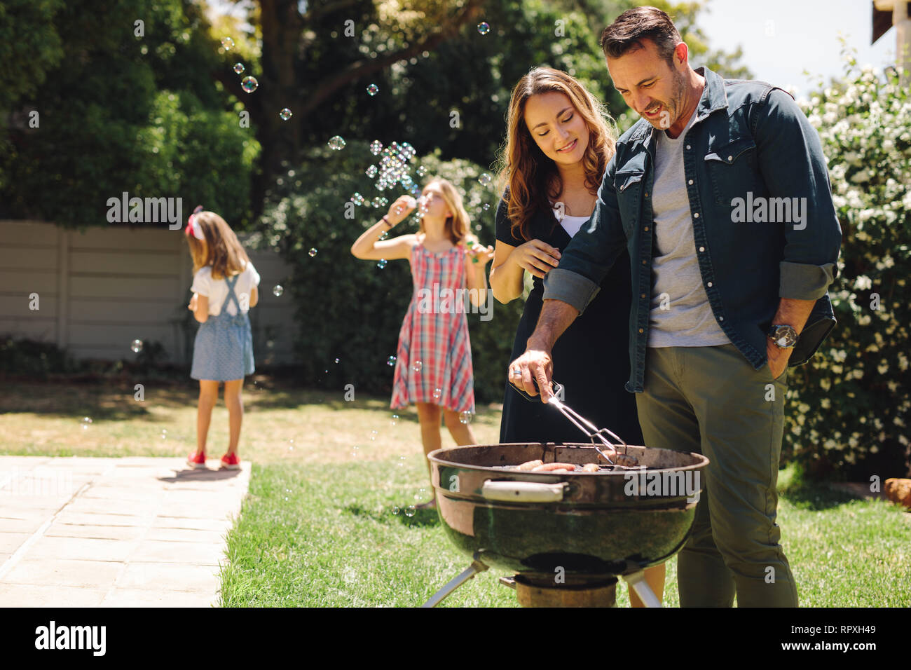 Happy man and woman making barbeque standing together in their backyard ...