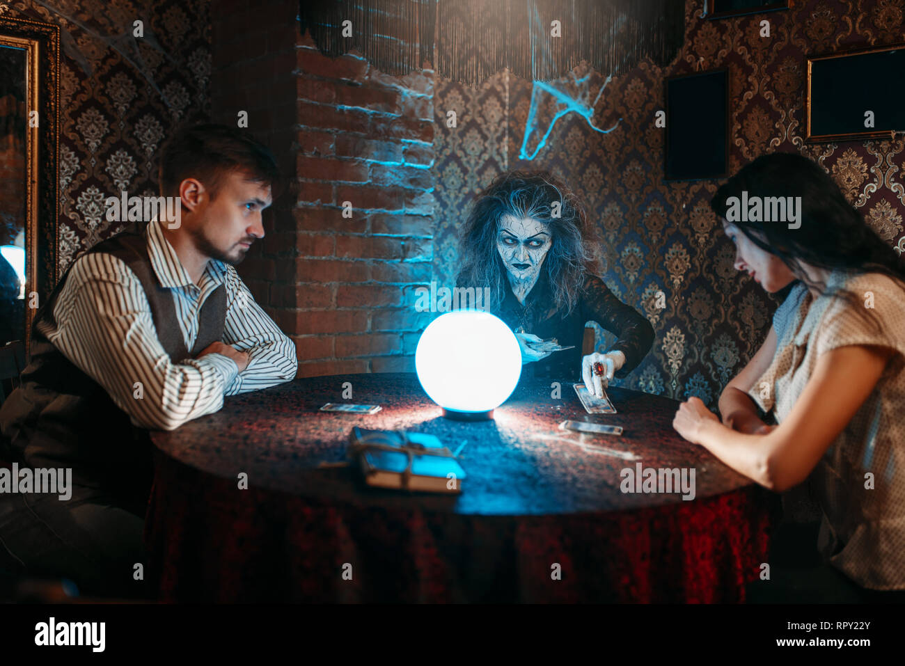 Witch reads a magic spell over a crystal ball, young couple on ...