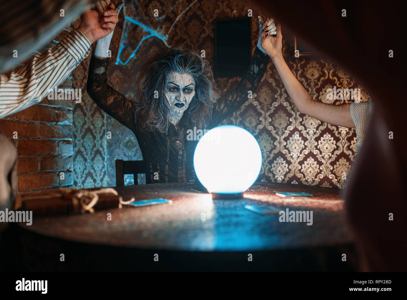 Scary witch reads a magic spell over a crystal ball, young people hands ...