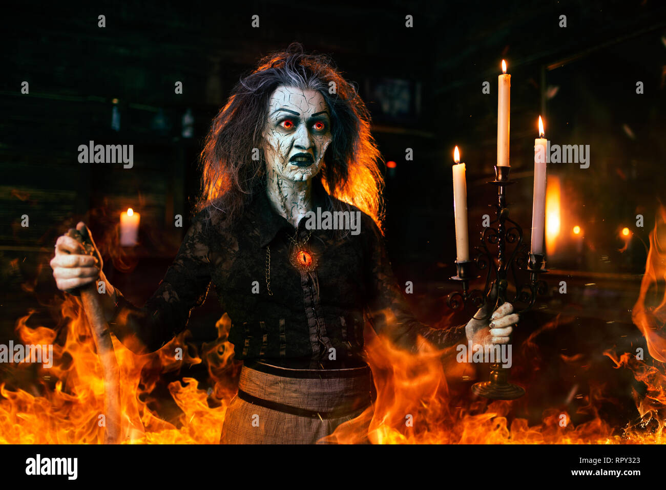 Scary witch with a cane at the mirror and candles, dark powers of ...