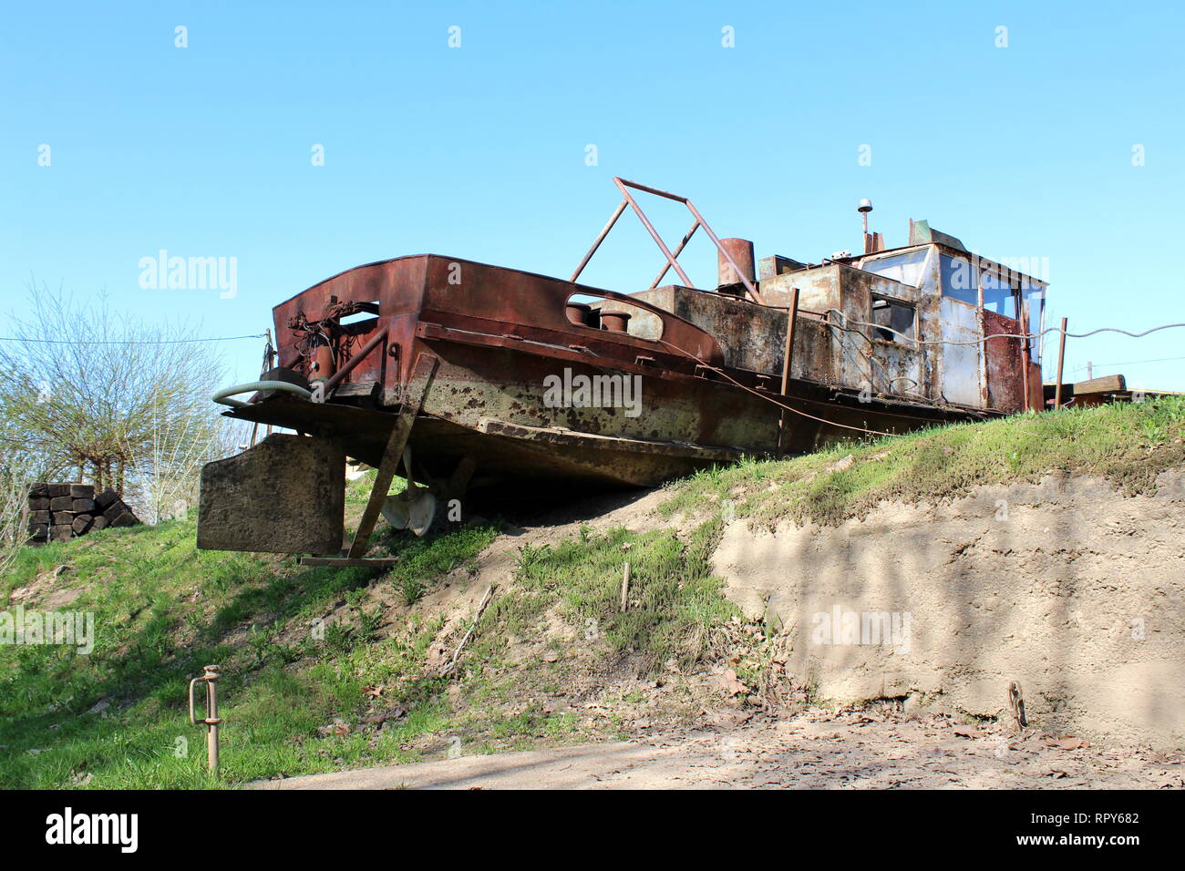 Rusted metal river barge left unused on edge of river bank surrounded ...