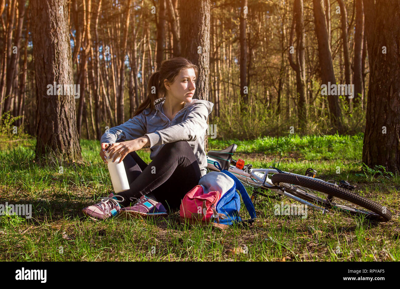 Woman having a rest after riding a bicycle in the forest at sunset ...